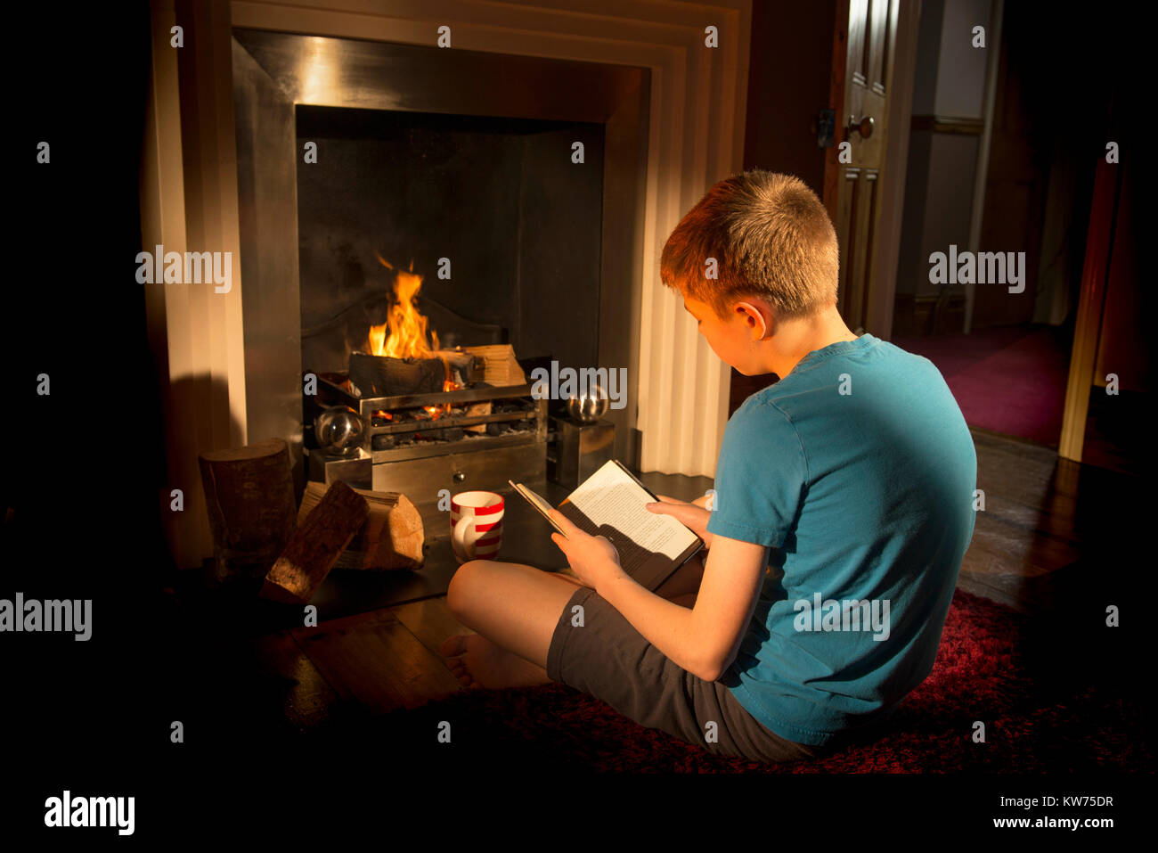 Teenage boy reading beside the fire. Hygge Stock Photo - Alamy