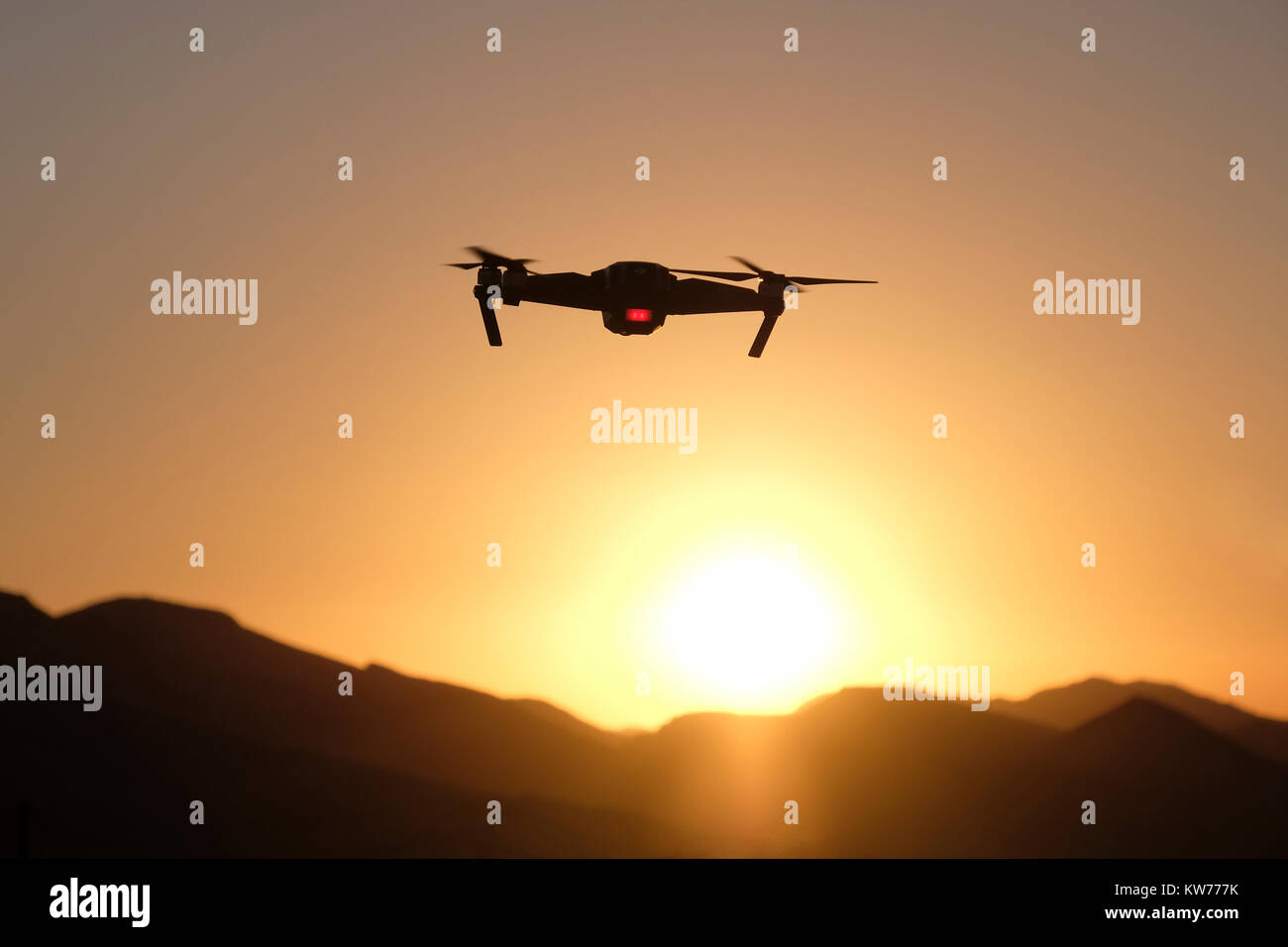 A camera equipped radio controlled quadcopter drone flying at sunset in ...