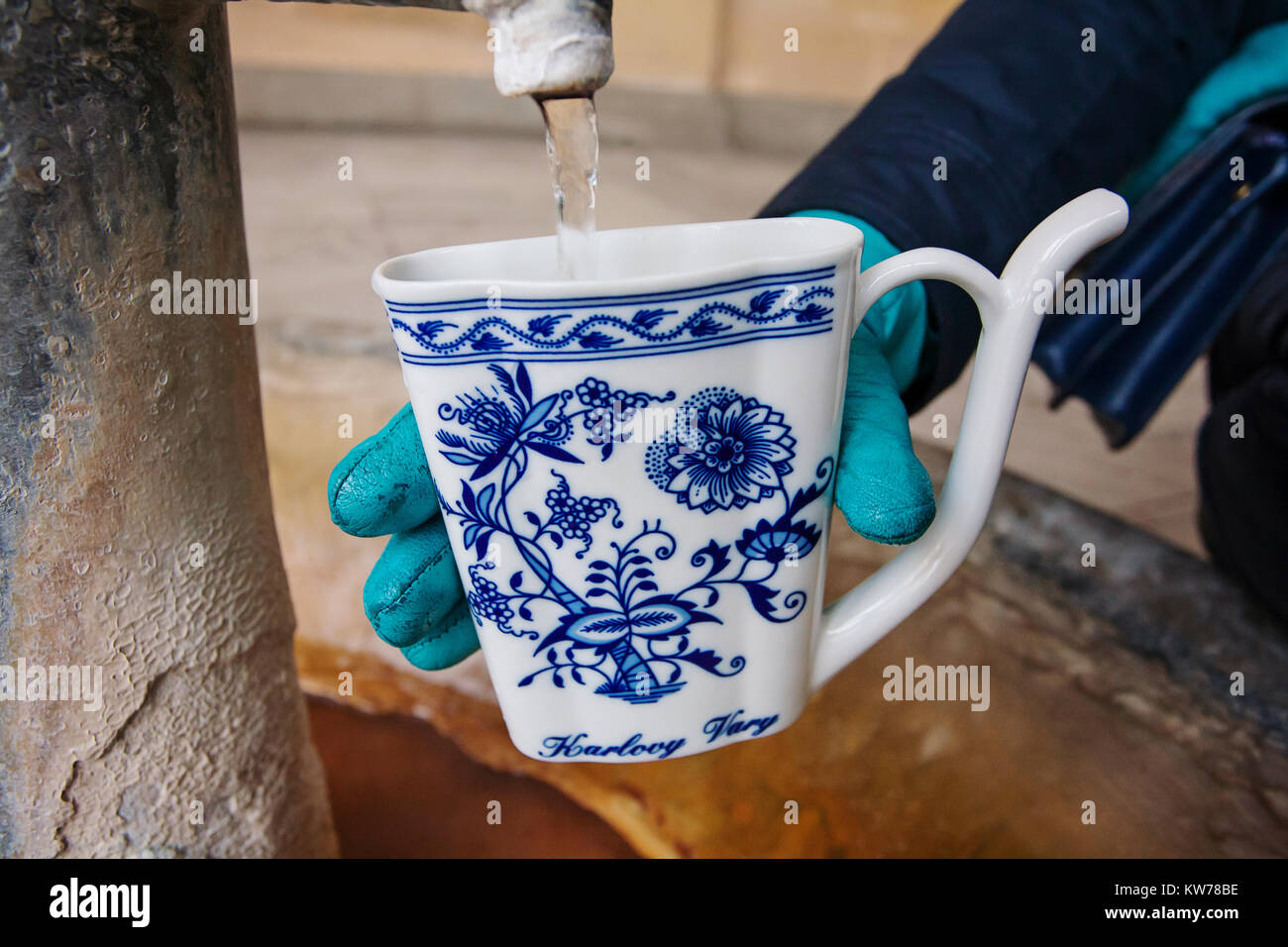 Hand in glove filling a cup with therapeutic mineral water at a natural ...