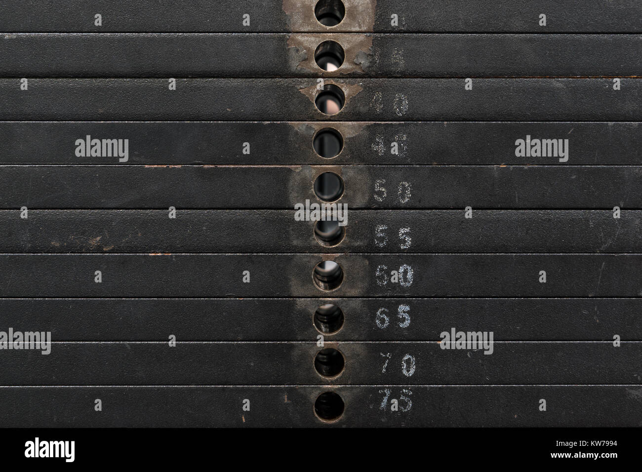 Old and used black weight stack with white numbers in a gym. Rusty flat ...
