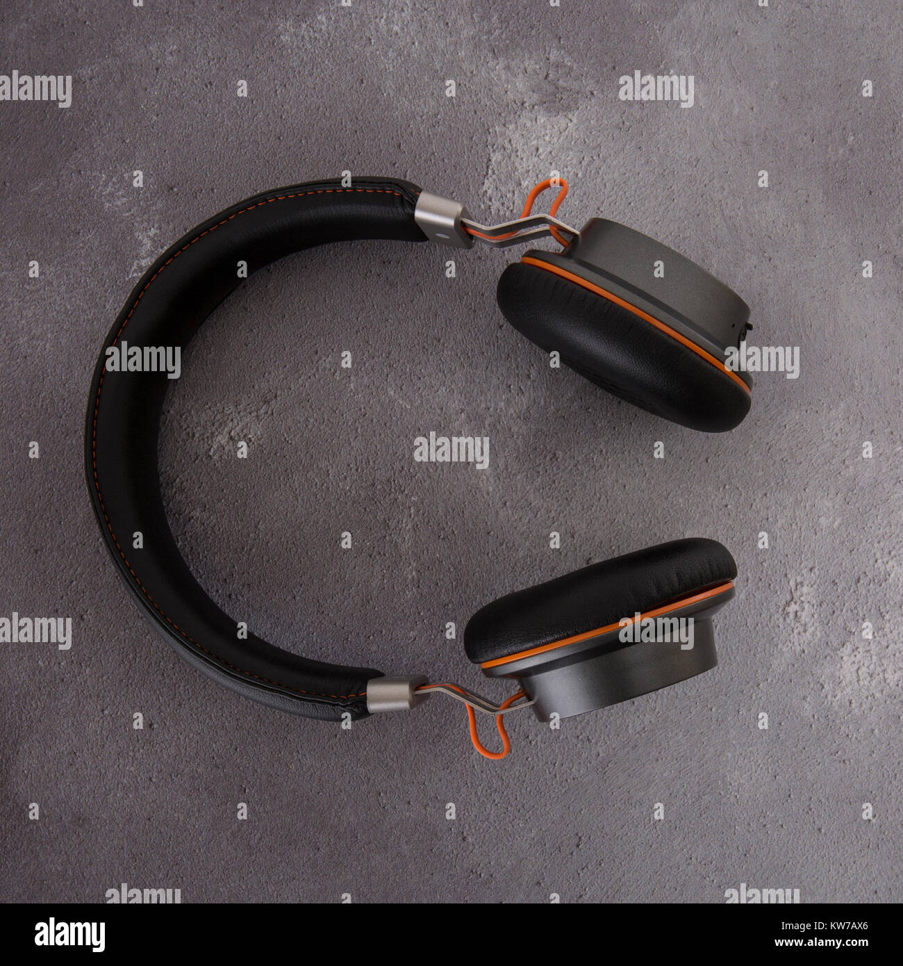 Pair of modern black and orange bluetooth headphones on a grey rustict ...