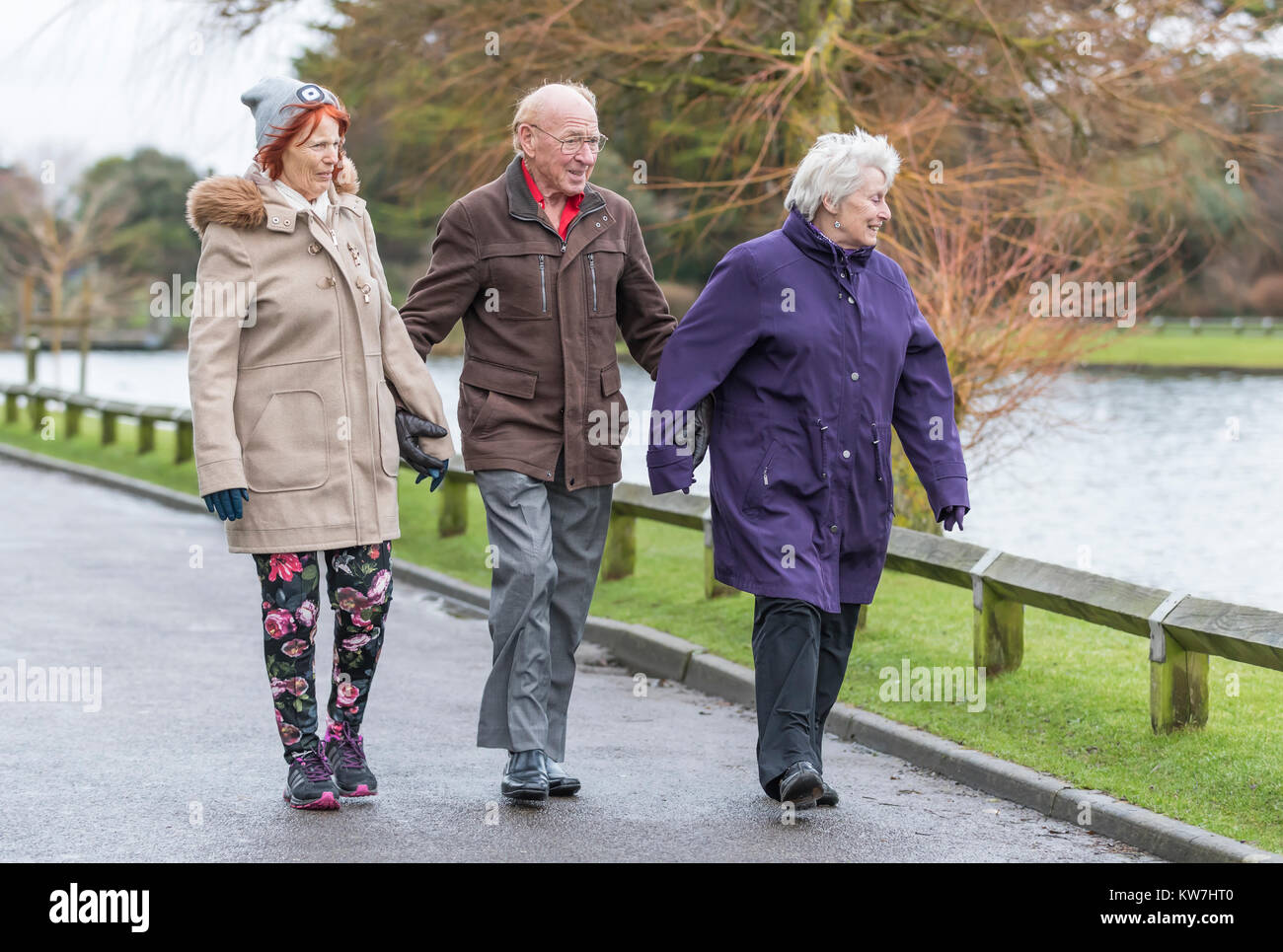 A man linking arms with 2 women while walking through a park in Winter ...