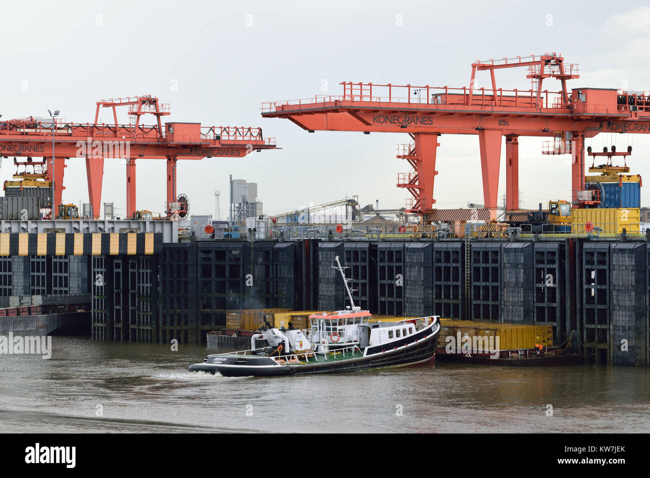 Gantry crane adjacent to river loading containers onto trucks with tug ...