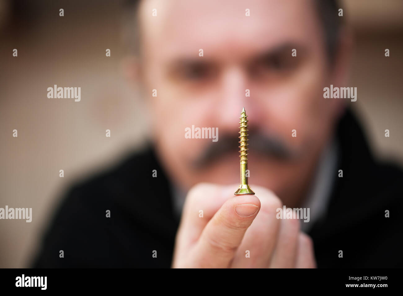 Man holding a screw on his finger and looking at it Stock Photo - Alamy