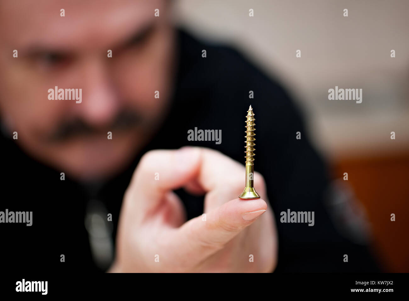 Man holding a screw on his finger and looking at it Stock Photo - Alamy