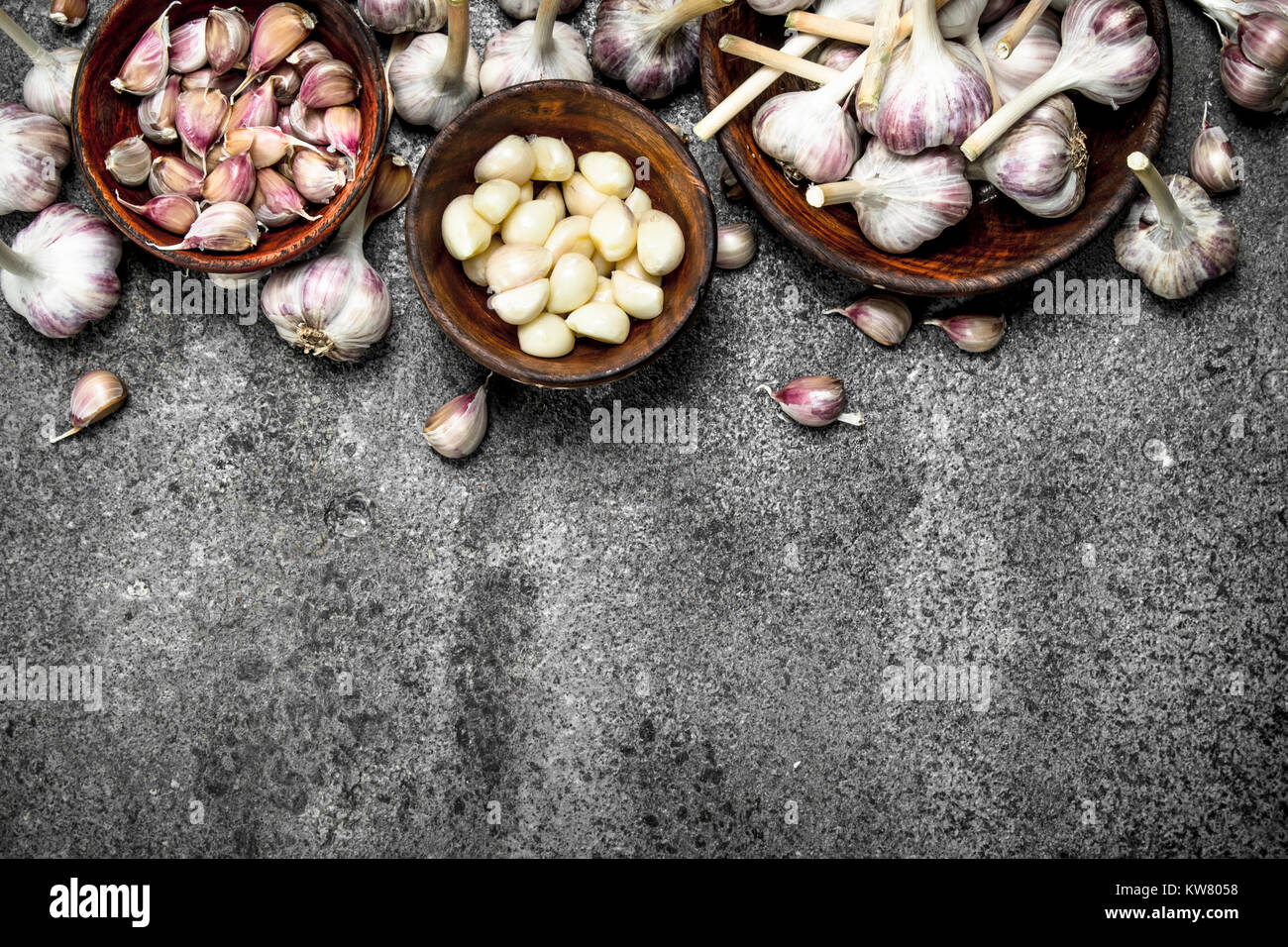 Peeled slices of fresh garlic in bowls. On a rustic background Stock ...