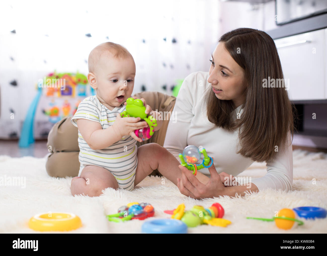 Funny baby and young woman playing in nursery. Happy family having fun ...