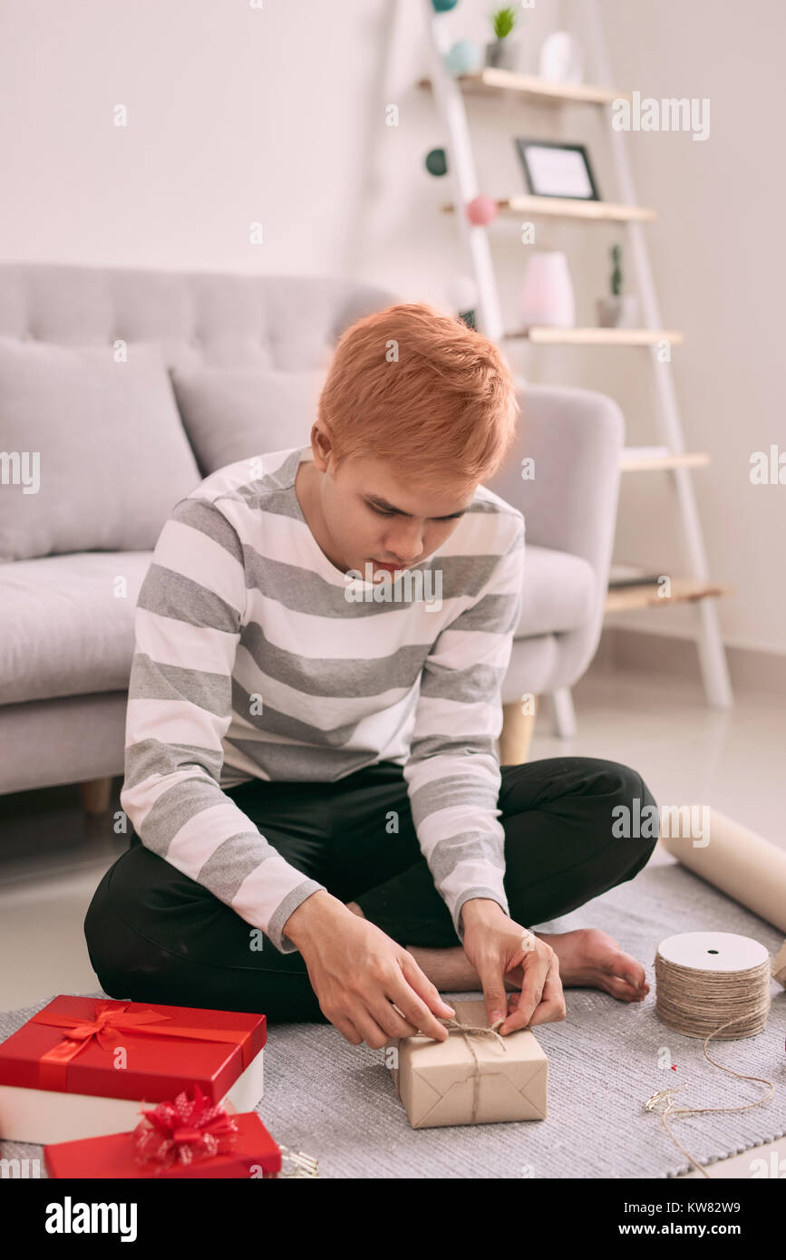Young happy man packing Valentine gift while sitting on floor Stock ...