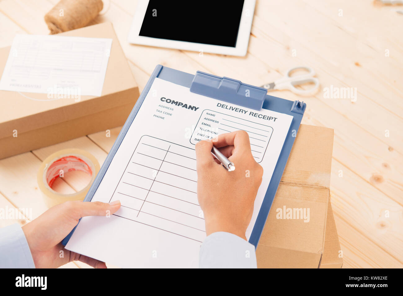 Courier making notes in delivery receipt among parcels at table Stock ...