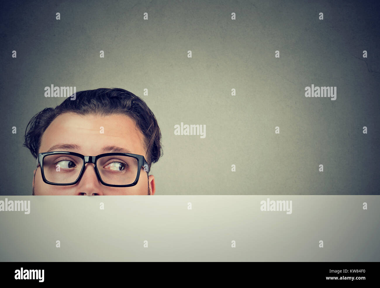Worried man peeking while hiding behind table looking away Stock Photo ...