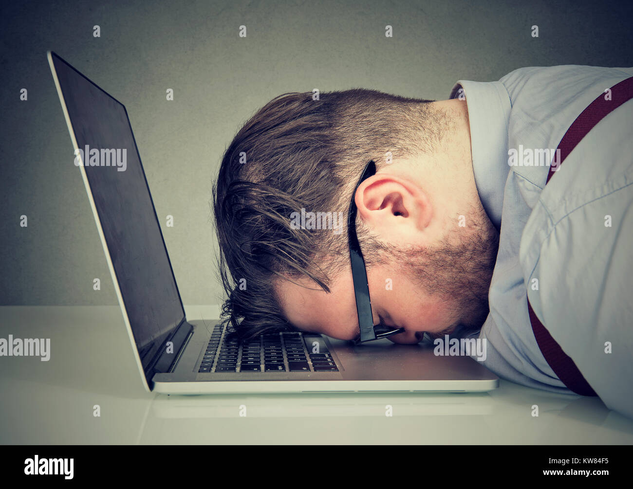 Side view of chubby man looking broken while lying on top of laptop ...