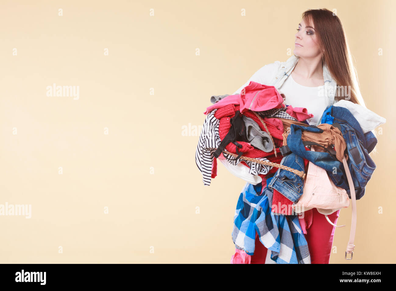 Young woman carrying stack pile of dirty laundry clothes. Girl cleaning tidying in studio ...