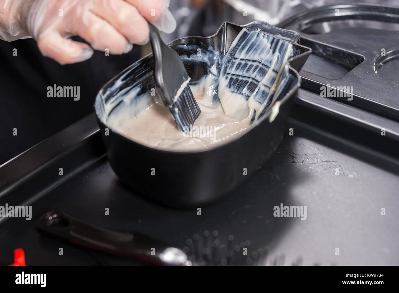 Close up of hands of female stylist mixes hair dye in paint container ...