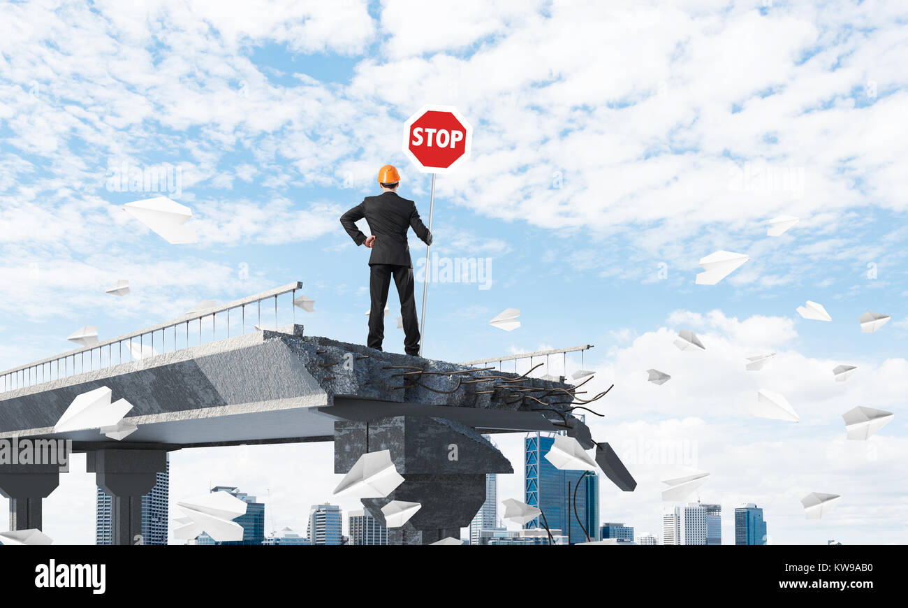 Rear view of engineer in helmet holding stop sign while standing among ...