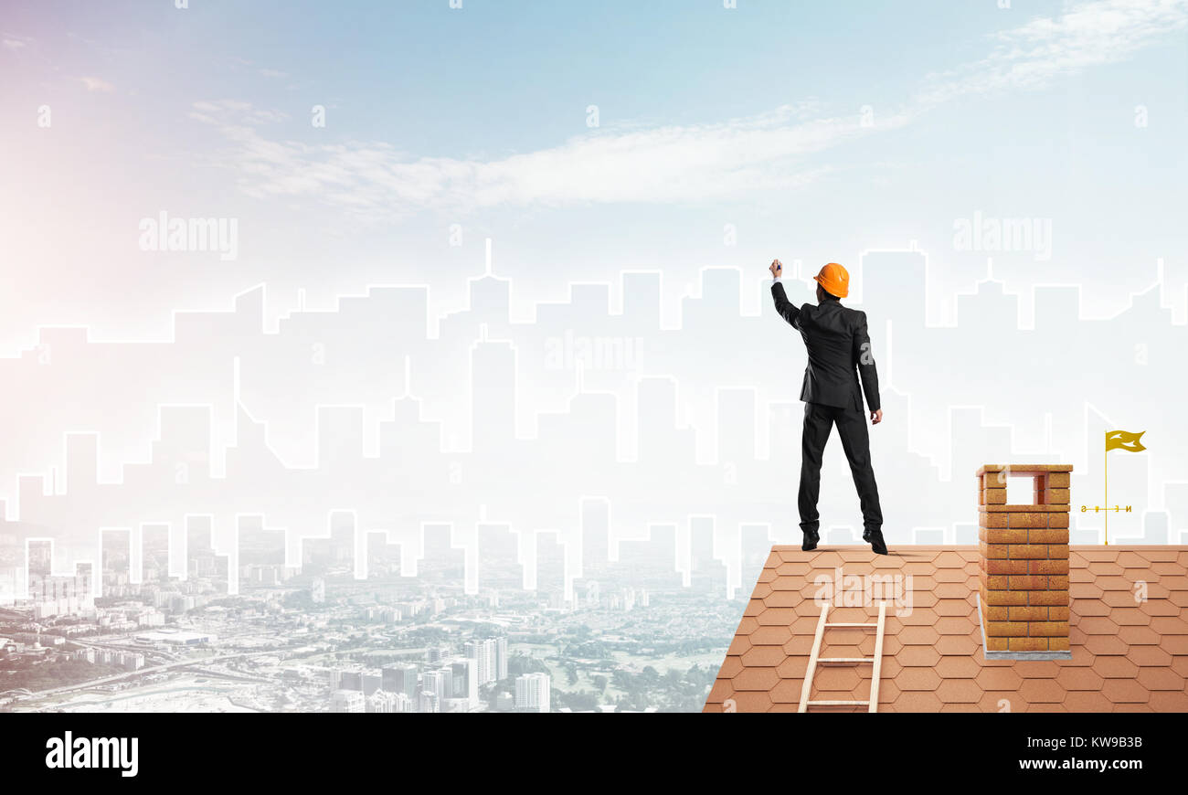 Engineer man standing with back on house roof and drawing city. Mixed ...