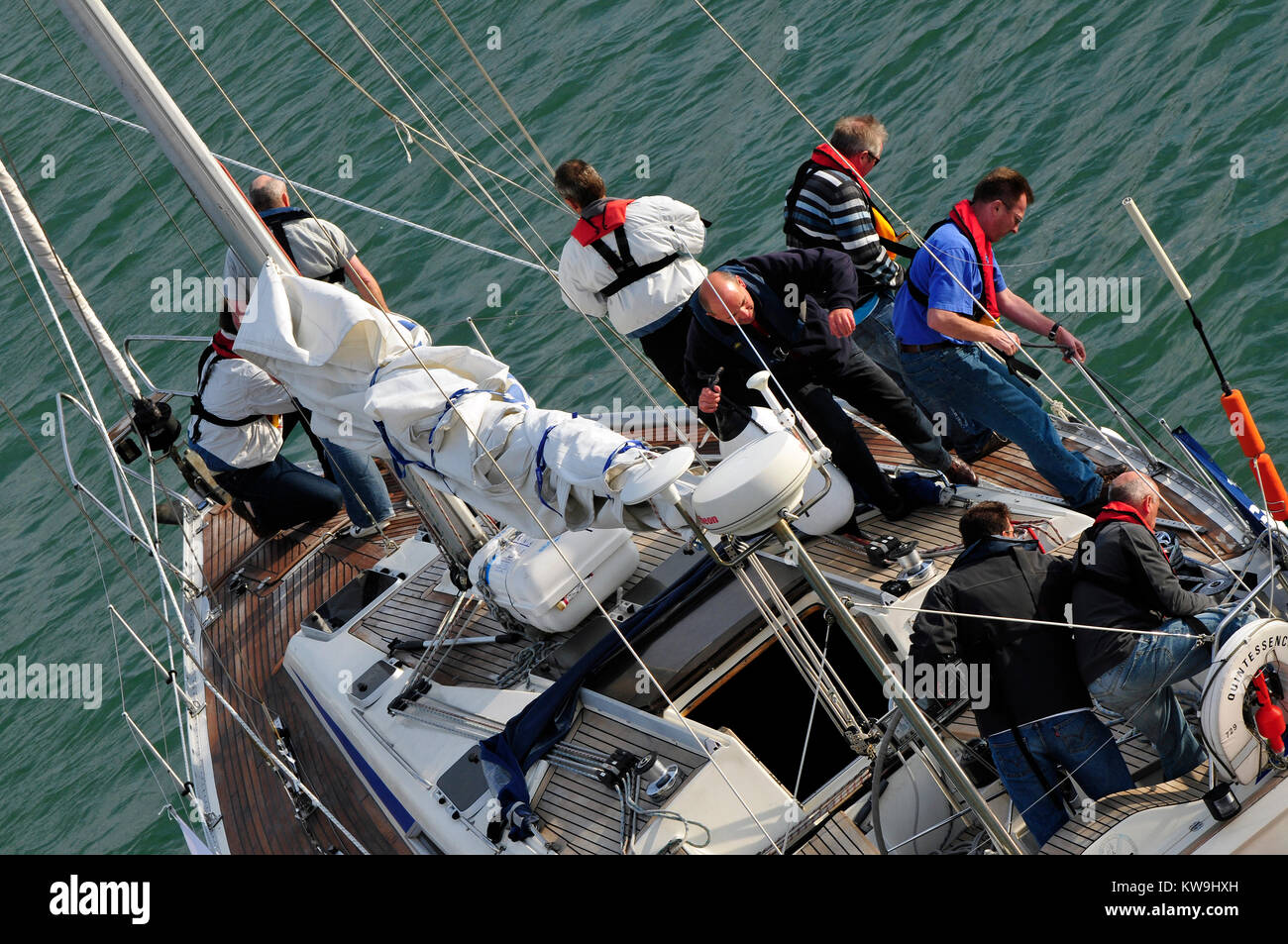 the crew of a large ocean going racing yacht busy carrying out various ...