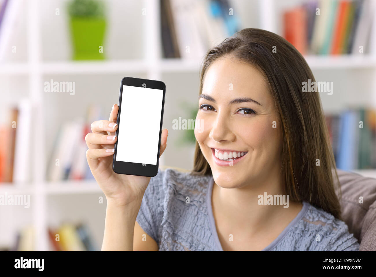 Happy lady showing a blank smart phone screen sitting on a sofa at home ...