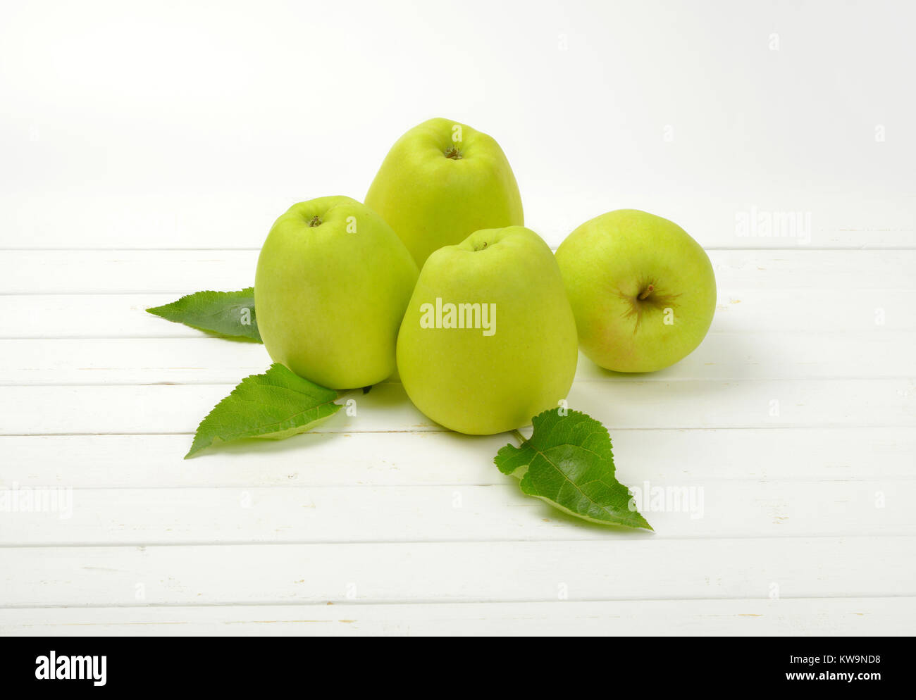 Four green apples with leaves on white wooden background Stock Photo ...