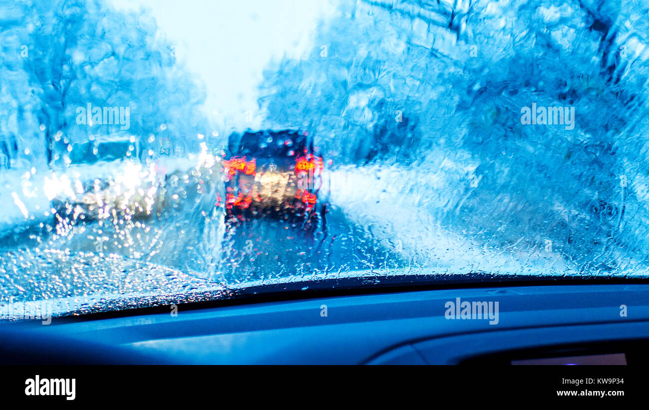closeup of front car window with raindrops and blurred heavy traffic ...