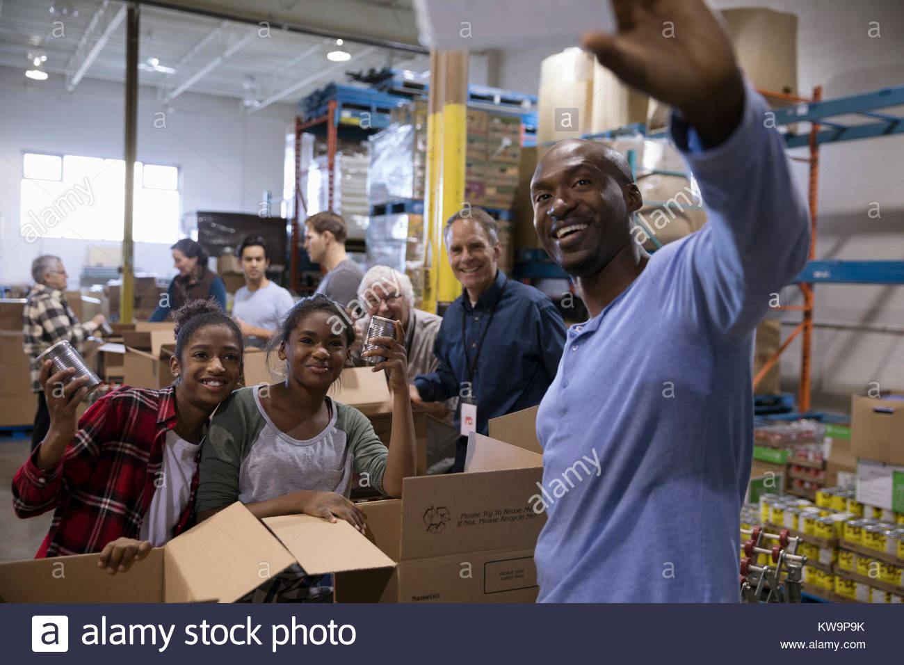 Volunteers boxing canned food for food drive,taking selfie in warehouse ...