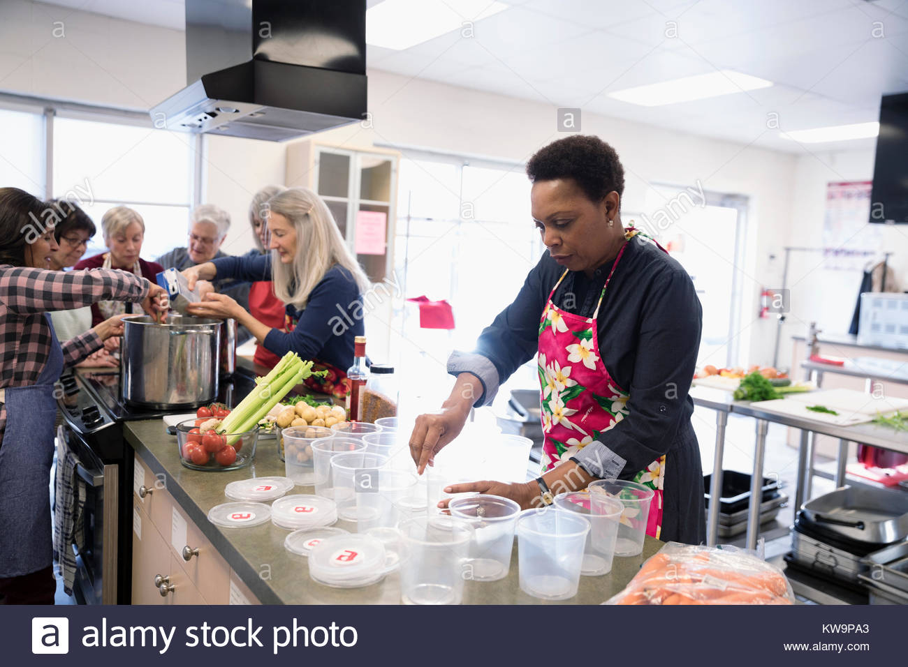 Female volunteers cooking in soup kitchen,preparing soup containers ...