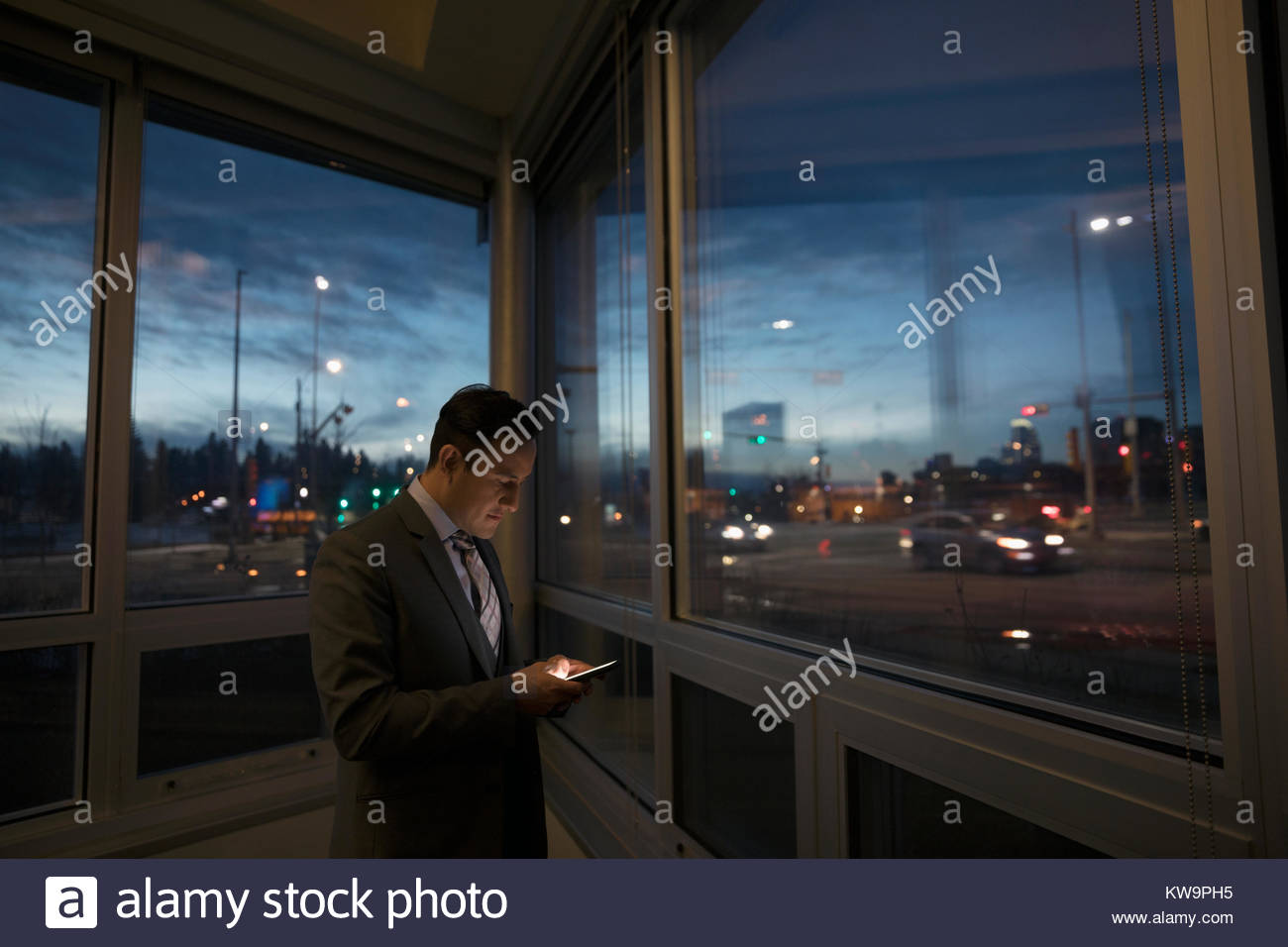 Businessman texting with smart phone at dark office window overlooking ...
