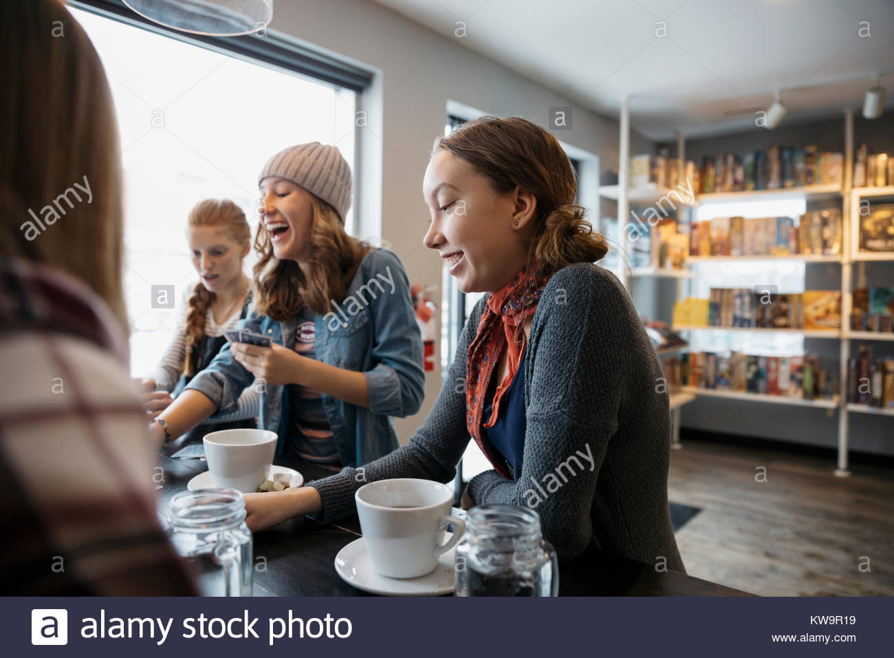 Tween girl friends playing cards and drinking coffee at cafe table ...