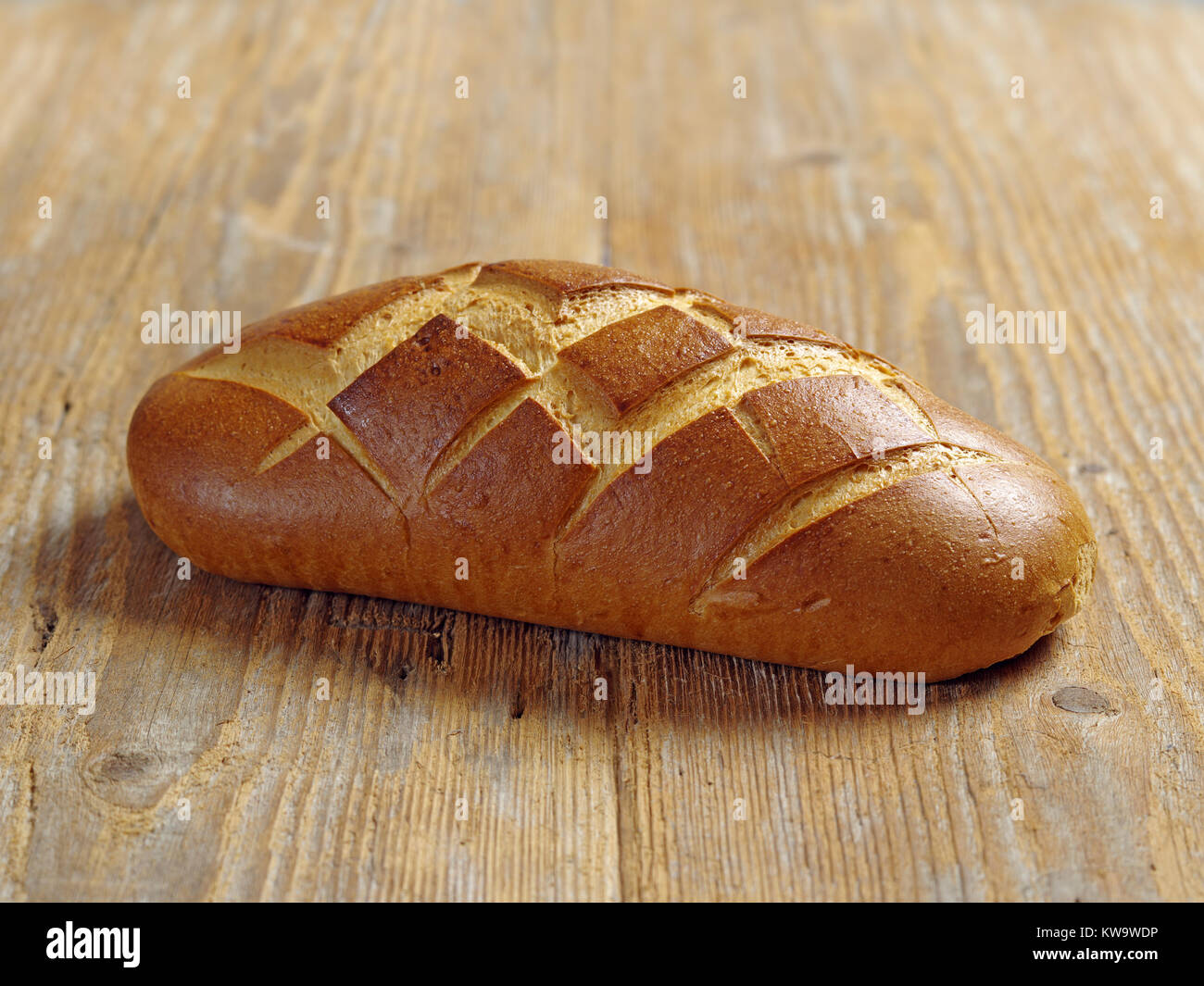Photo of a single loaf of uncut bread resting on an old wood table ...