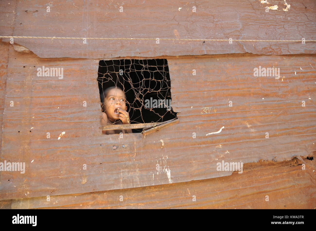 A kid looks at the sky through a narrow window in a shanty house at ...