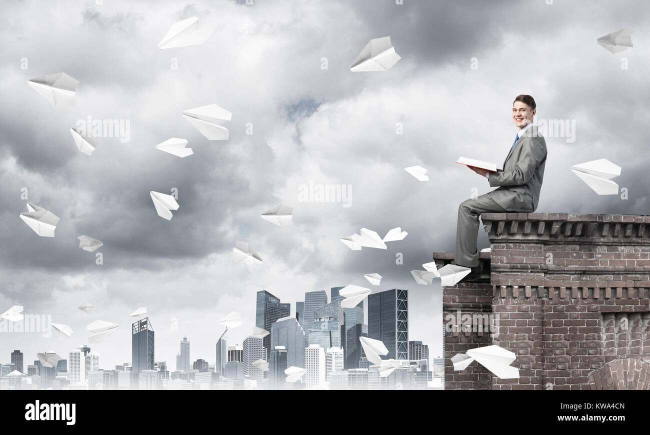 Young businessman sitting on building top with red book in hands Stock ...