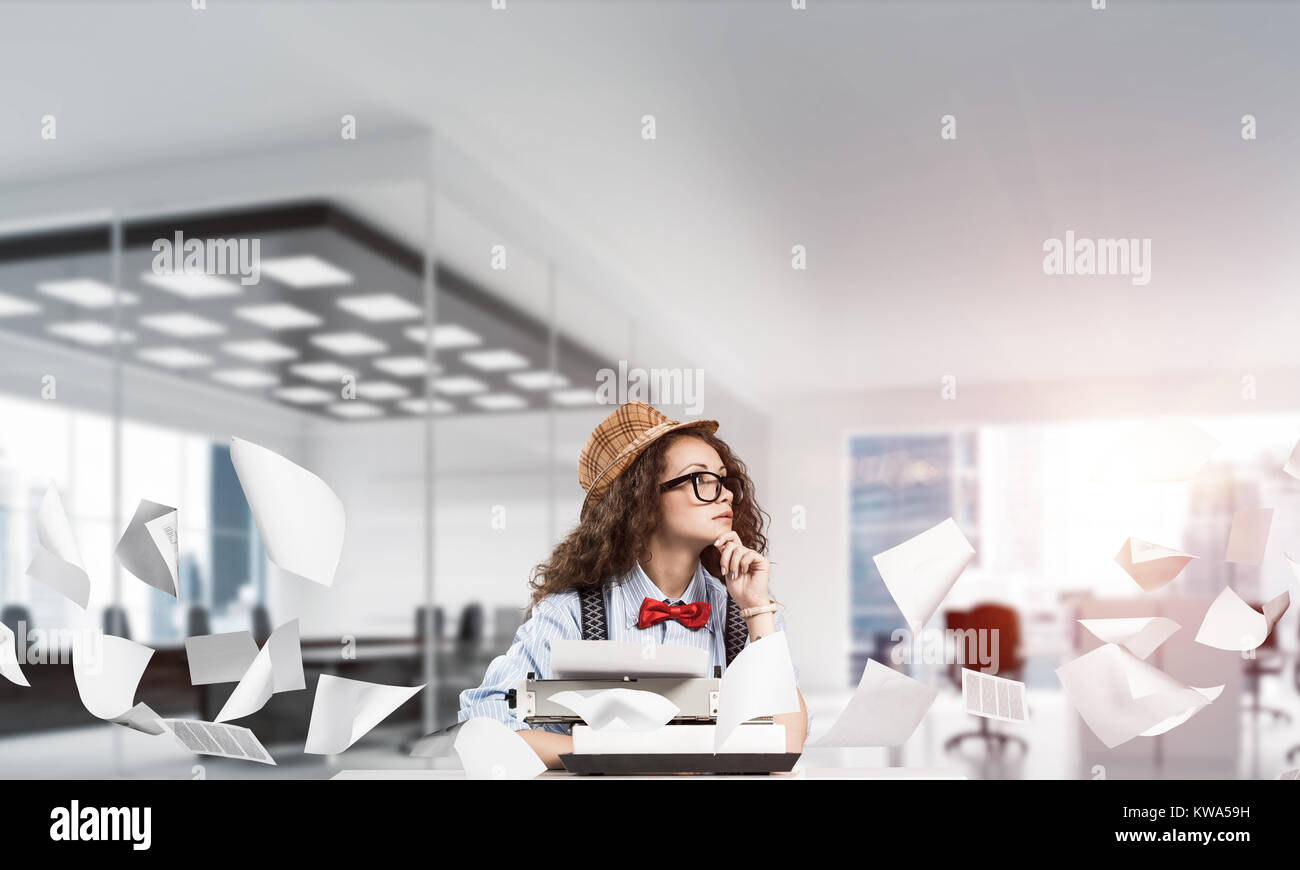 Young woman writer in hat and eyeglasses using typing machine while ...