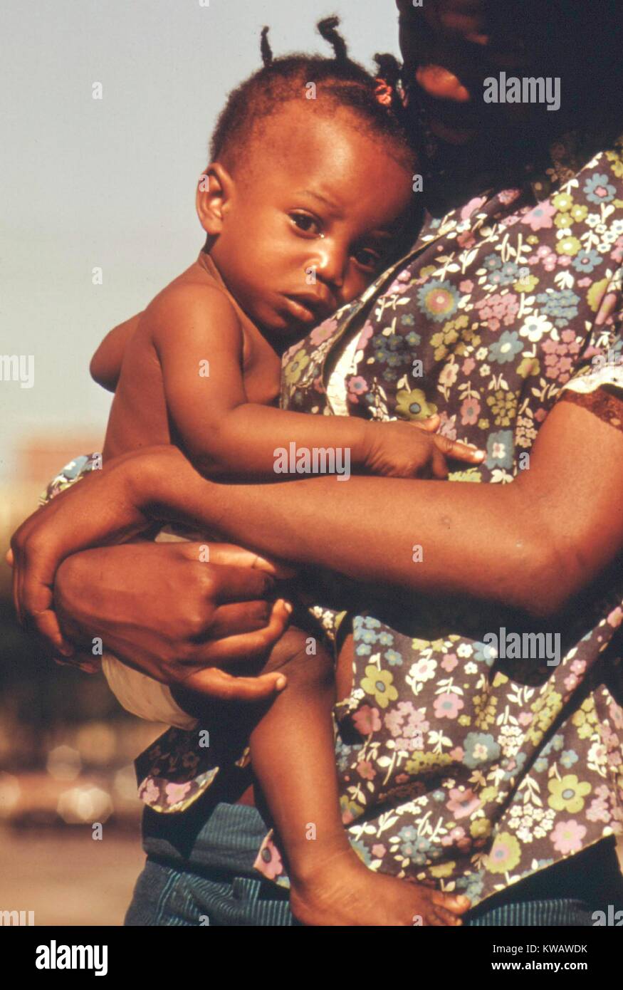 A low income mother cradles her infant daughter in the bright sun in ...