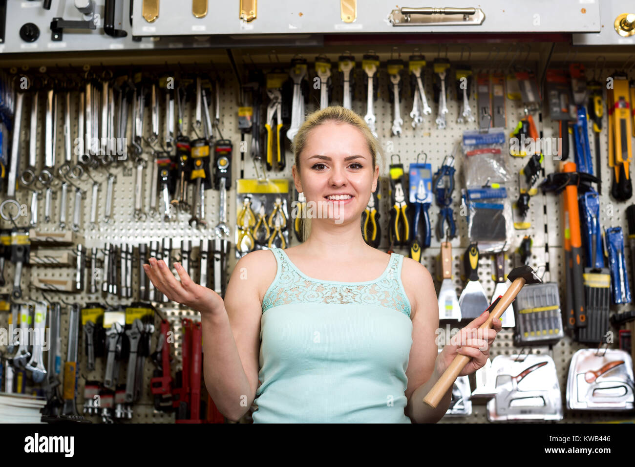 Portrait of young happy woman at the cash desk holding hammer in tool ...