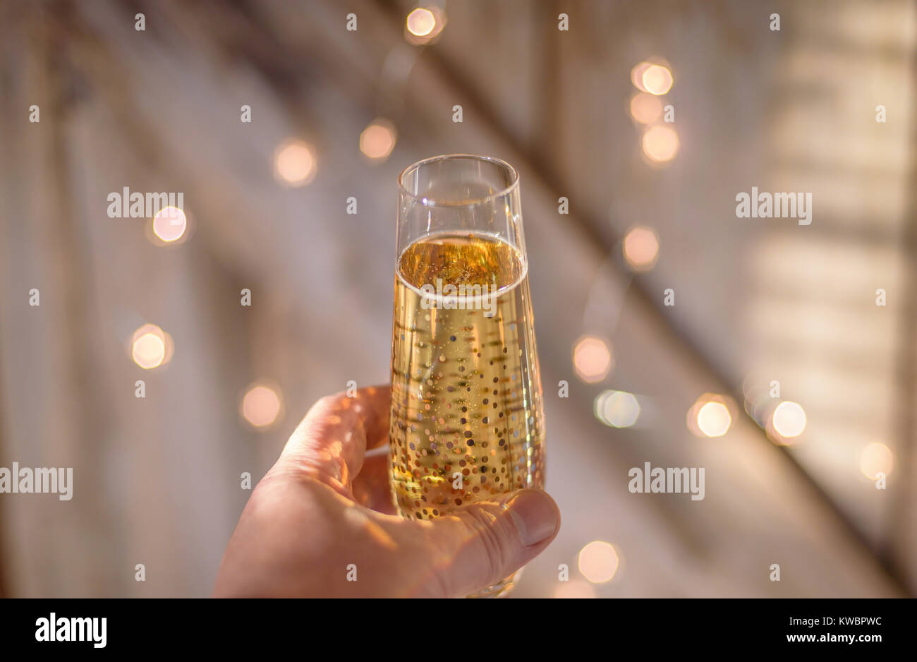 hand rasing a glass of champagne for a toast with twinkling lights in ...
