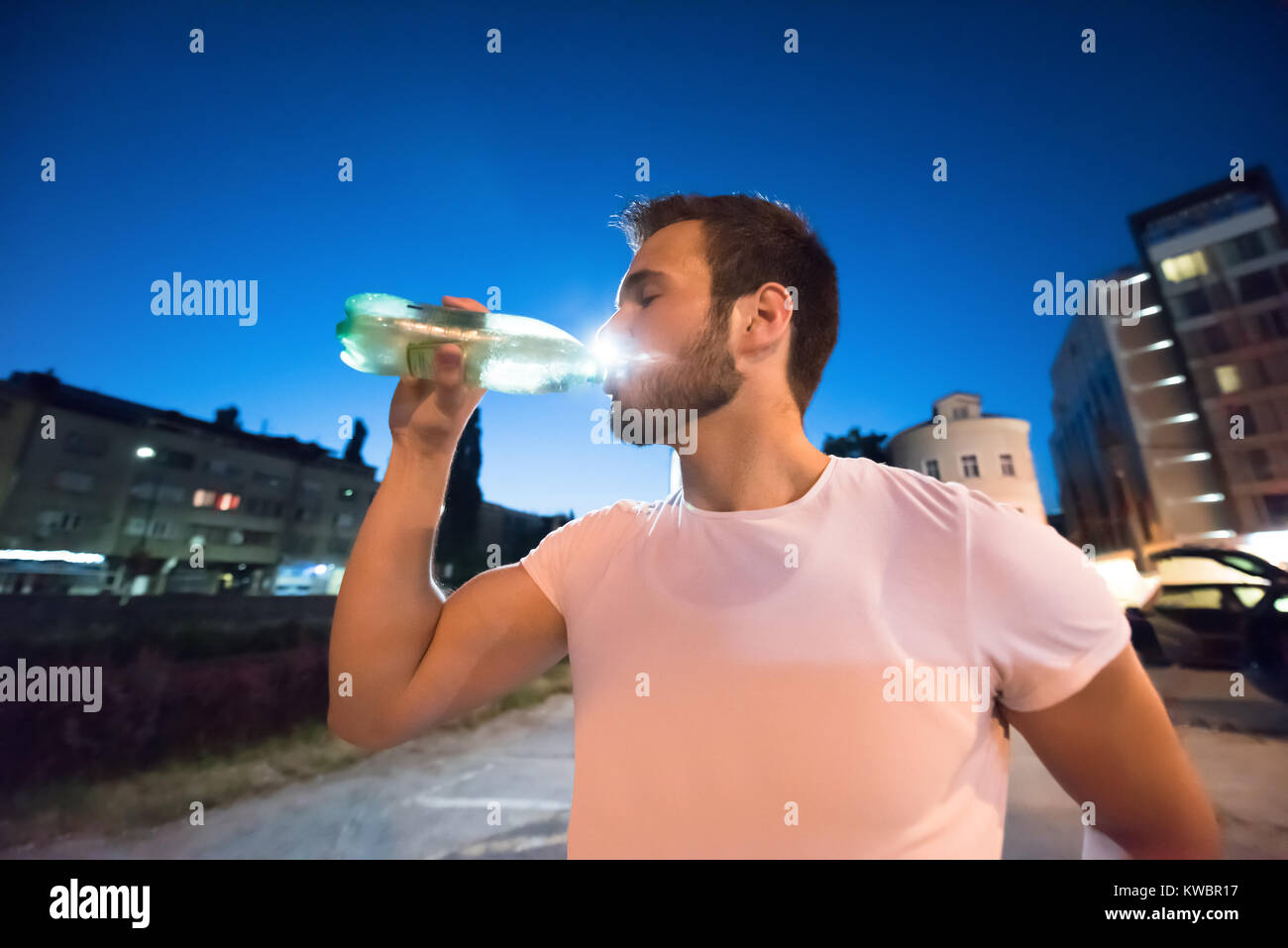 young athletic man drinking water after a night running session in the ...