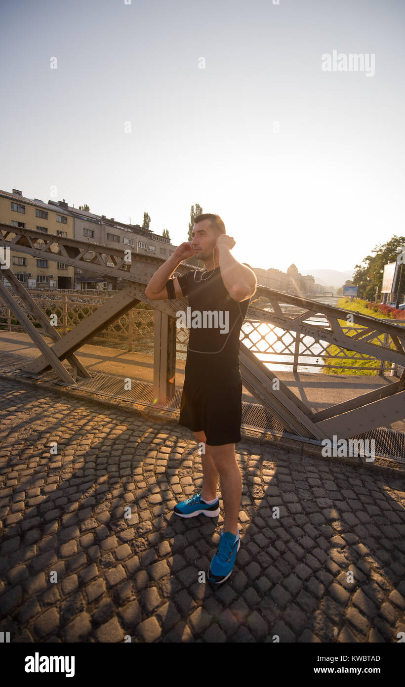 portrait of a young sporty jogging man at sunny morning in the city ...