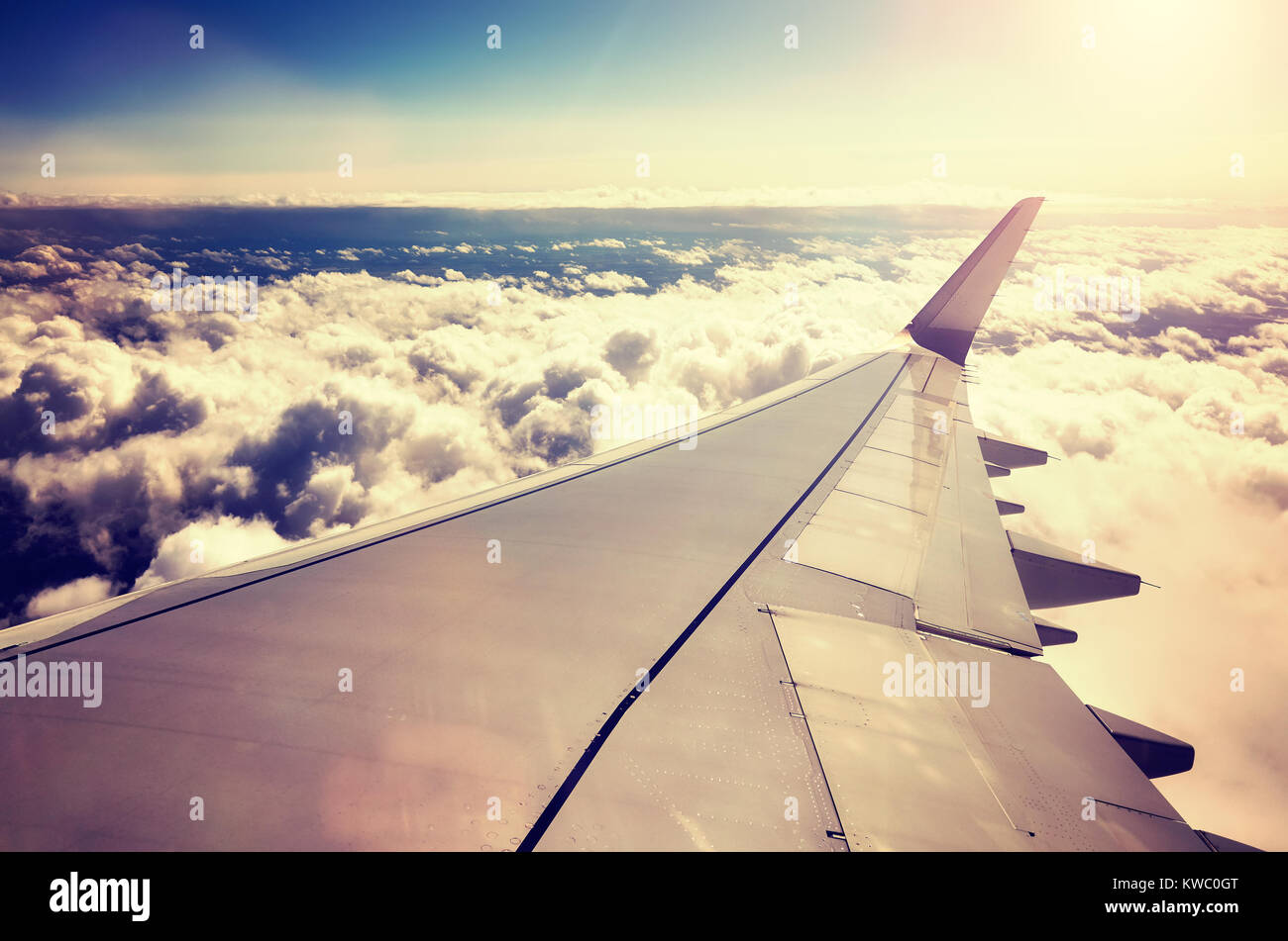 A plane wing above the clouds at sunset seen through a window of an ...