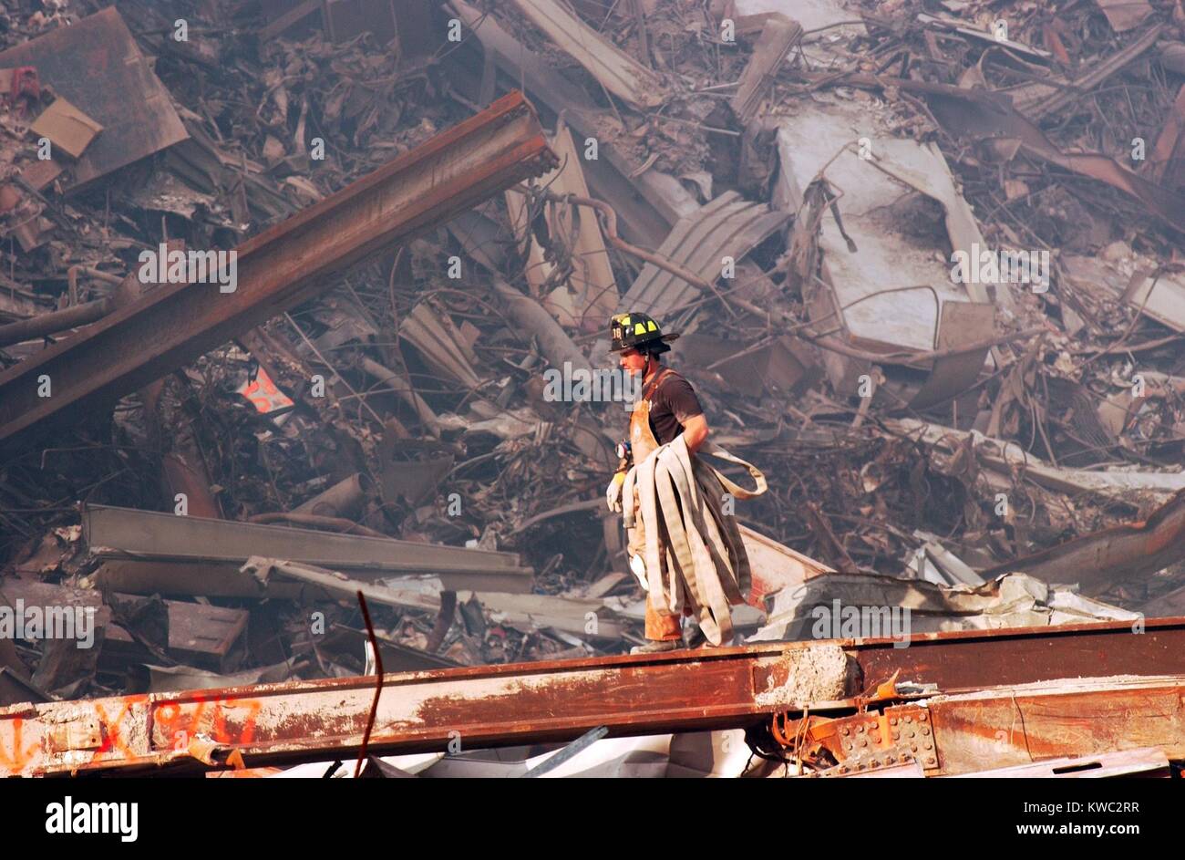 NYC Fire fighter carries a fire hose over smouldering fires and ...