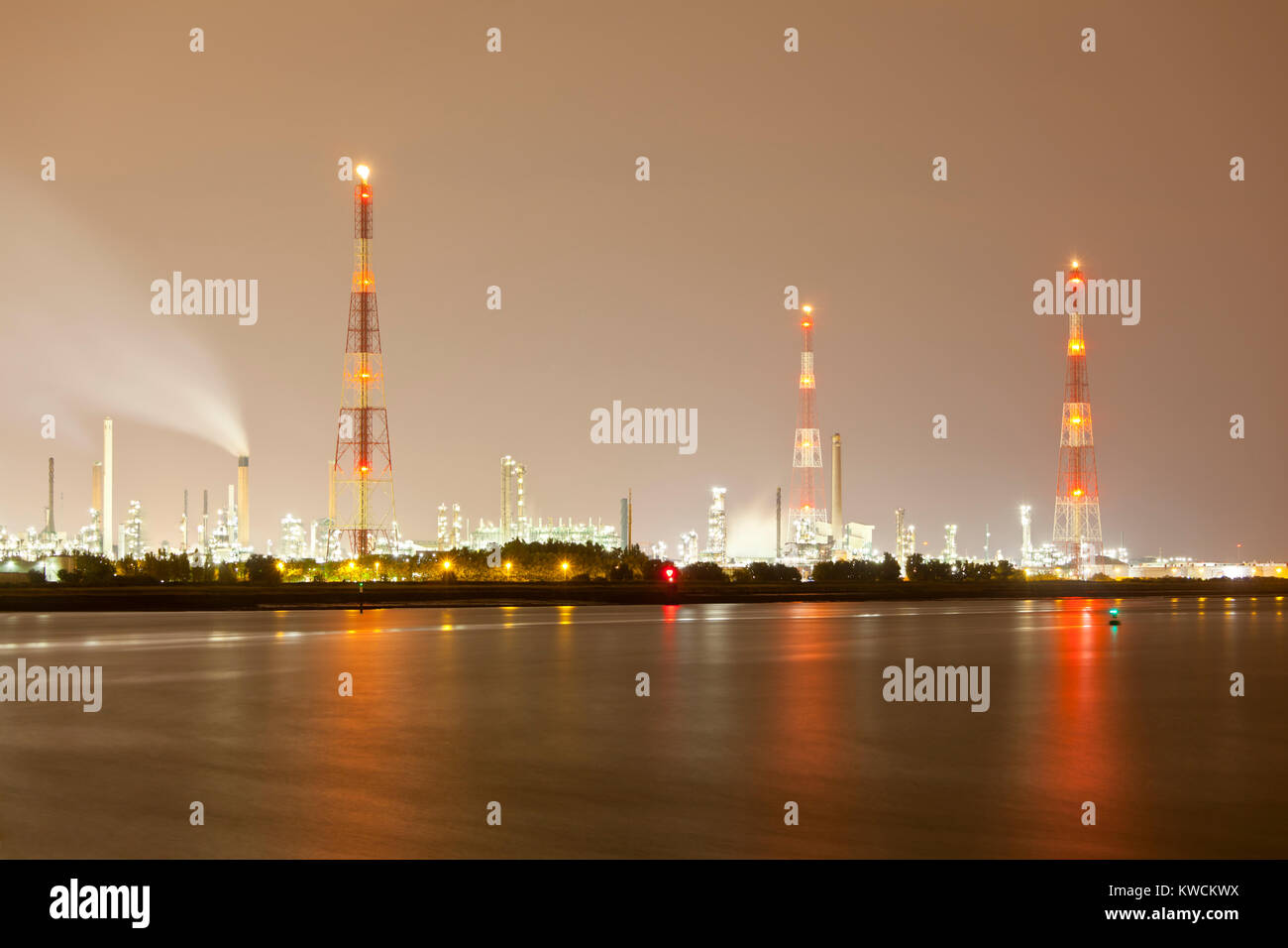 An oil refinery with tall gas flare stacks in a harbor with dirty night ...