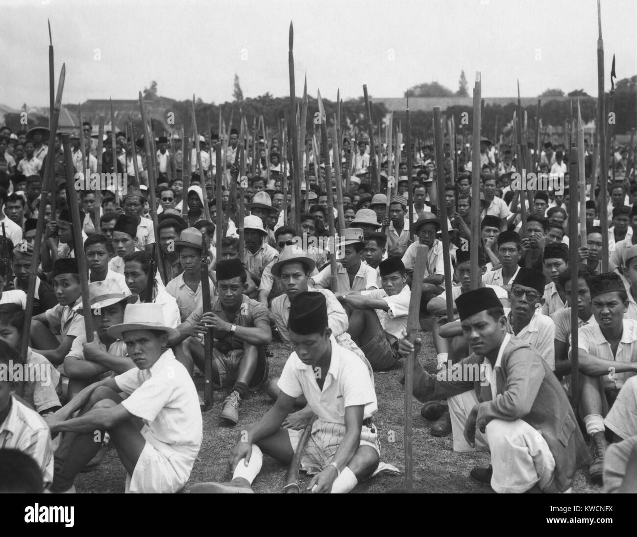 Young Indonesian men seated on ground holding sharpened bamboo poles ...