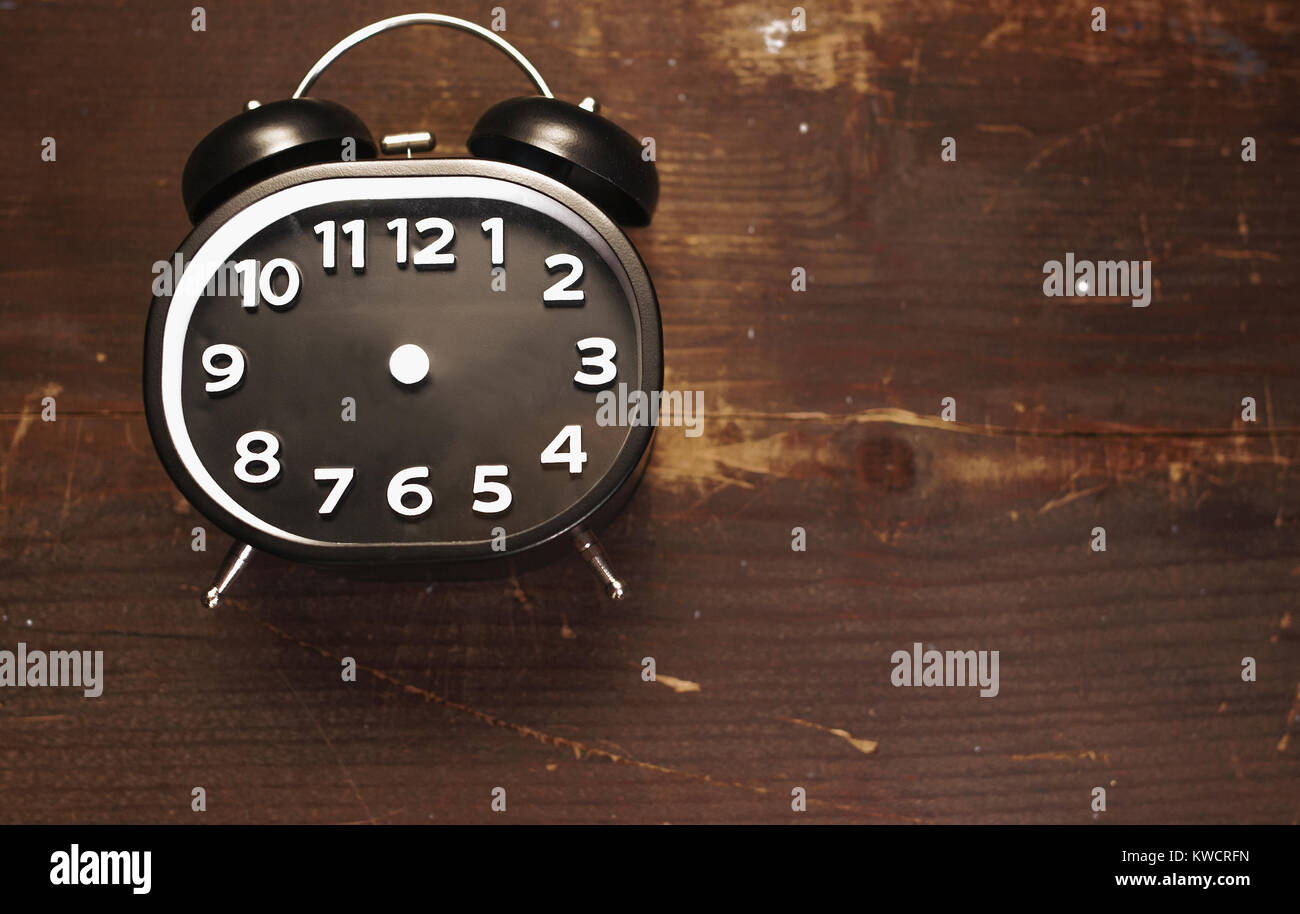 a black and white vintage alarm clock laying on a wooden background ...