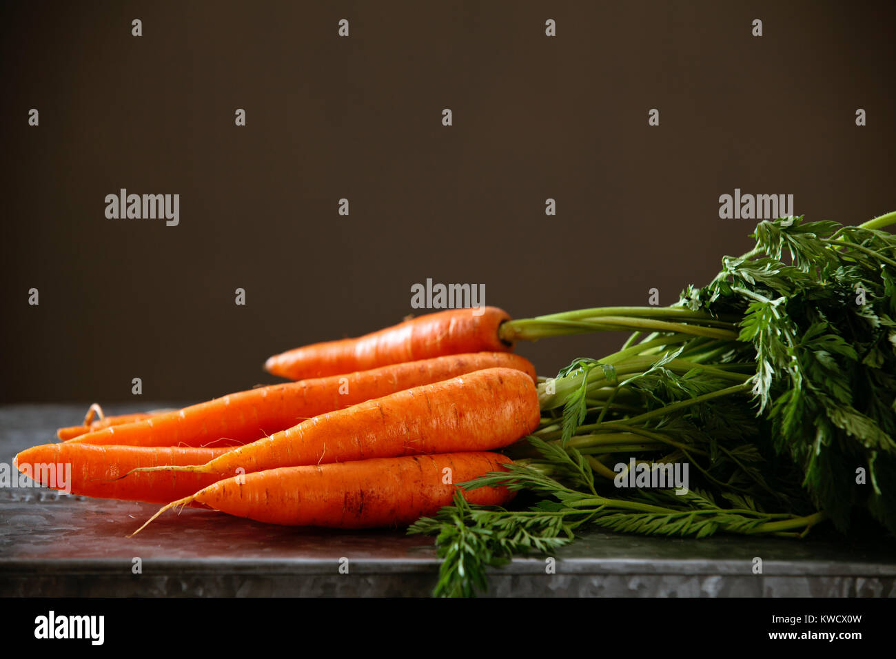 Heap of ripe carrots with leaves on dark rustic table Stock Photo - Alamy