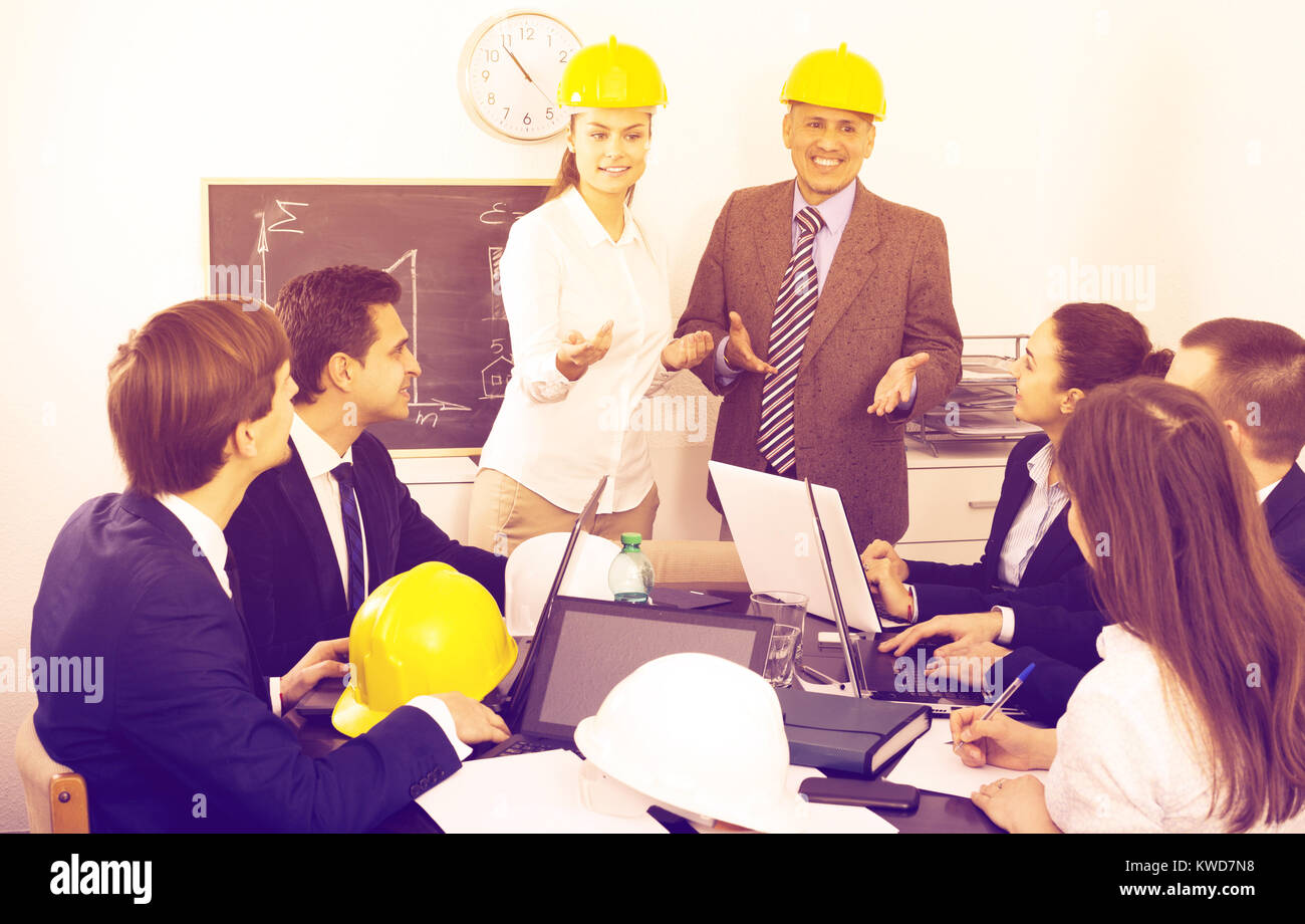 Positive professionals with laptops and helmets having presentation of ...