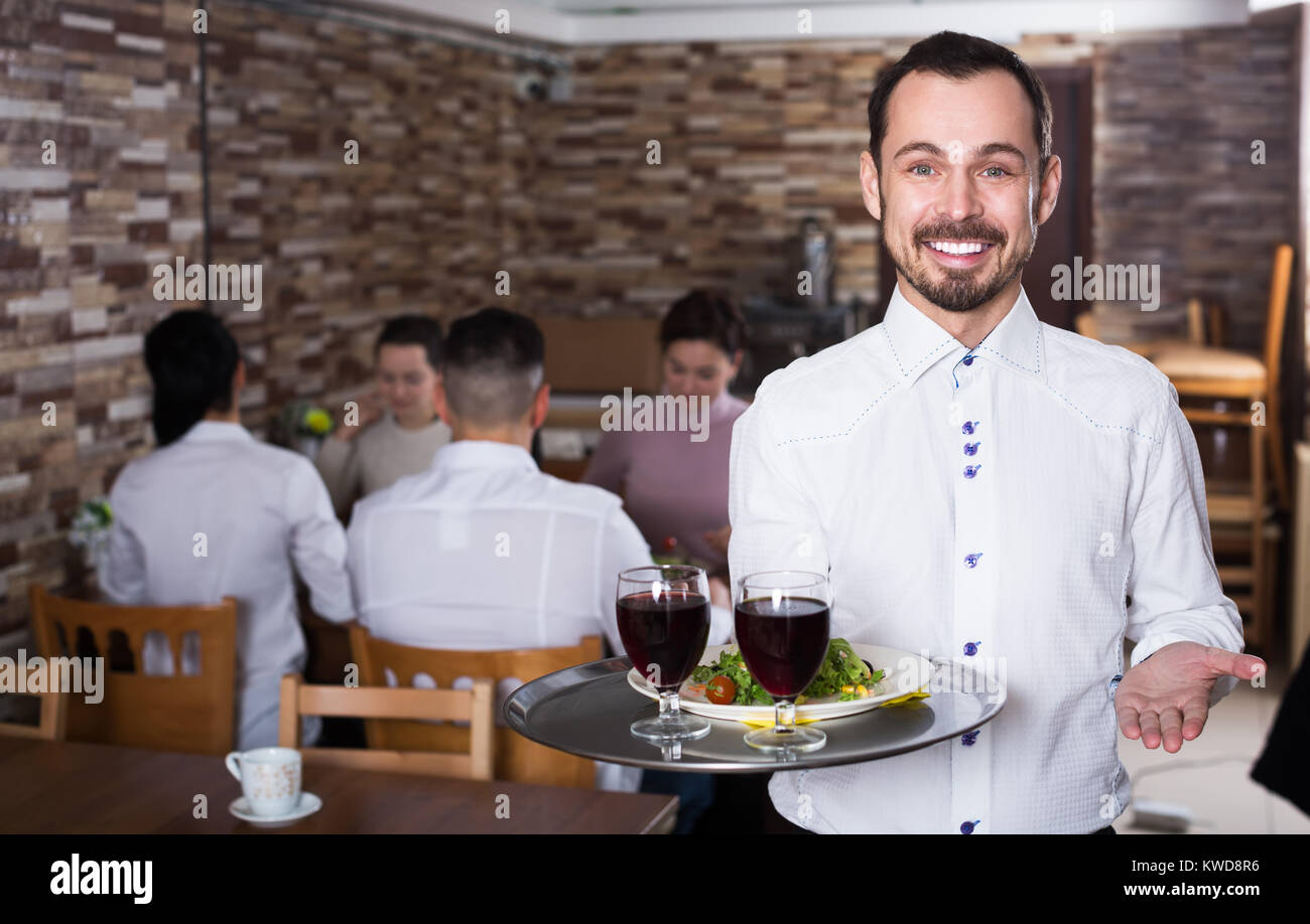 Smiling man waiter demonstrating country restaurant to visitors Stock ...