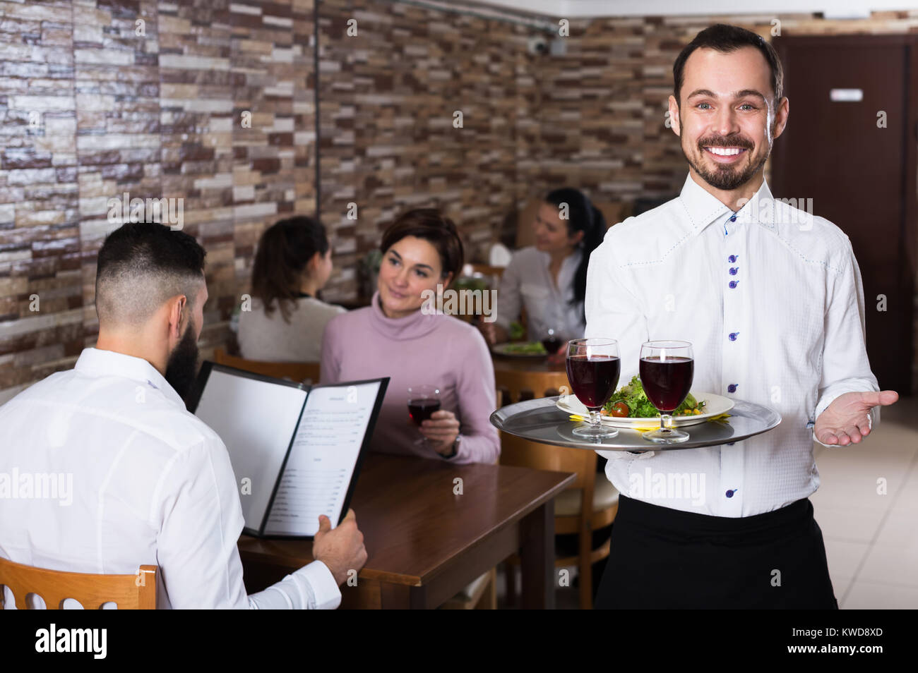 Positive male waiter showing rustic restaurant to visitors Stock Photo ...