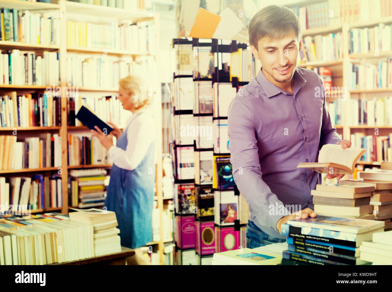 Young cheerful man holding open book in hands and looking at it in book ...