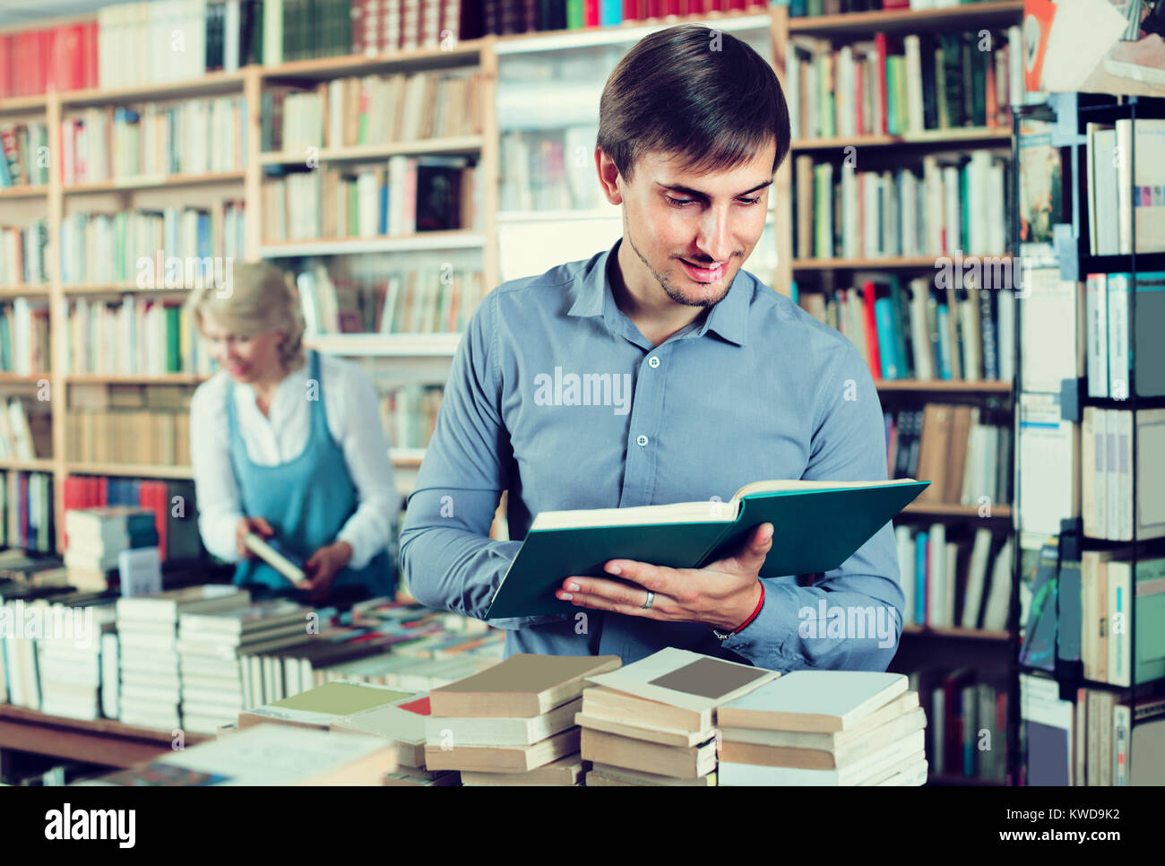 portrait of positive man looking at open book standing among ...