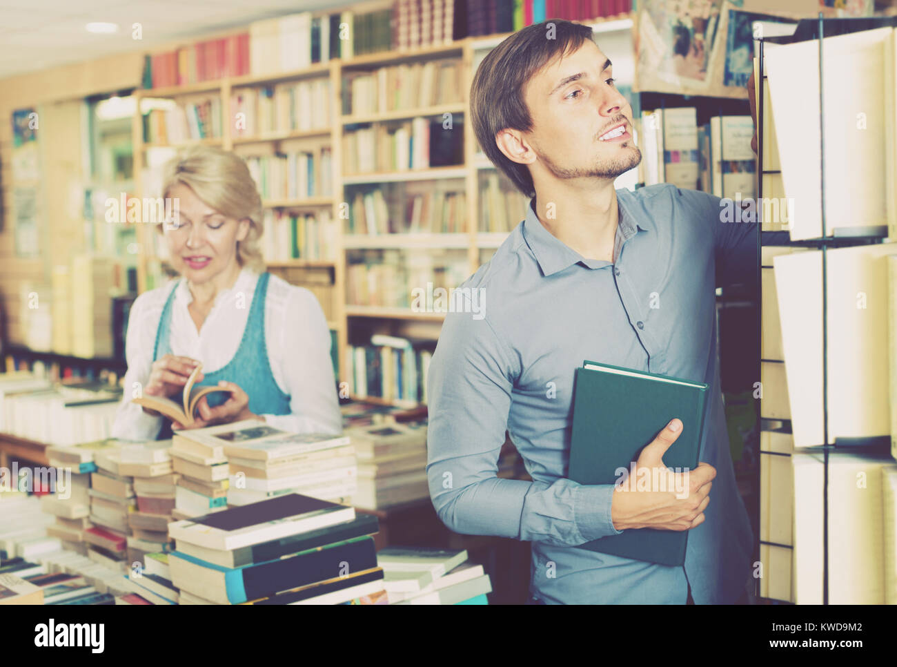 portrait of joyful young man standing among bookshelves and searching ...