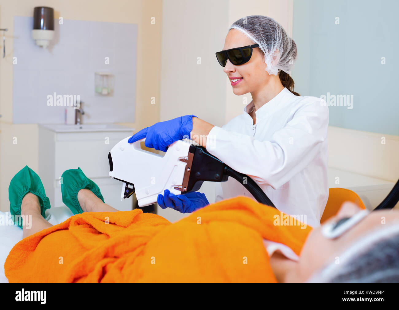 Young friendly smiling female client doing laser hair removal from legs ...