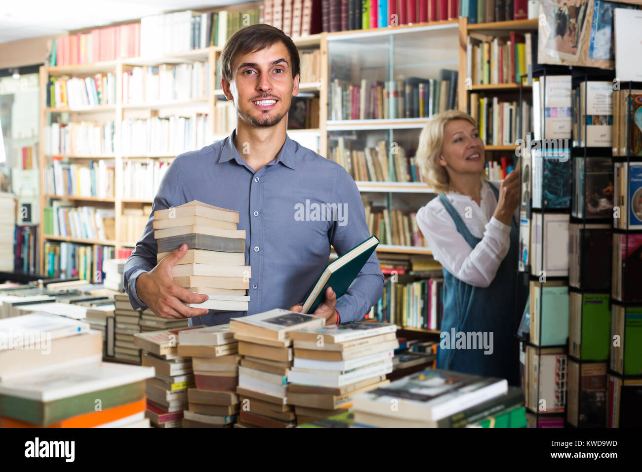 positive smiling young man holding pile of book in hands in book store ...